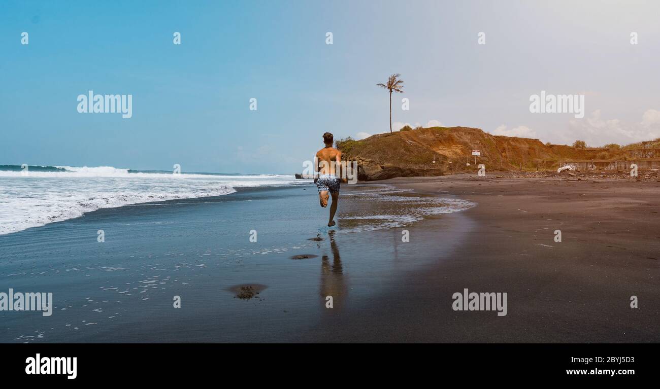 Sporty fitness man runner running on sunrise beach. Empty beach in Bali ...