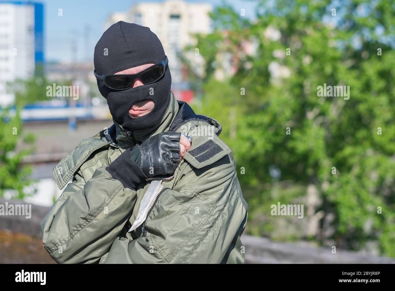 A thug in black glasses and a balaclava with a knife is plotting ...
