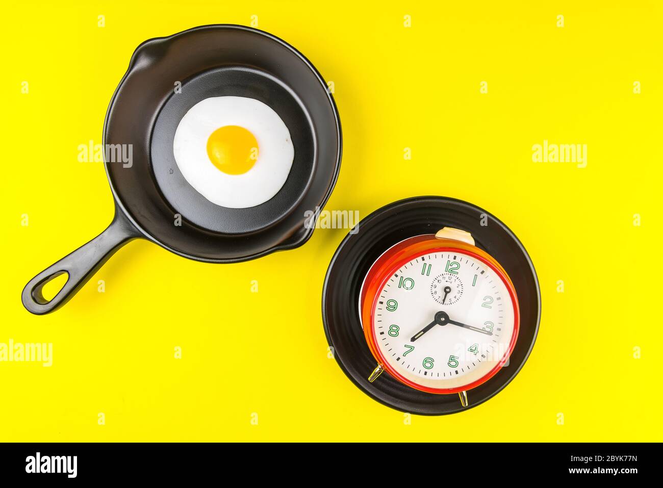 Frying pan with fried egg and alarm clock in a black plate isolated on ...
