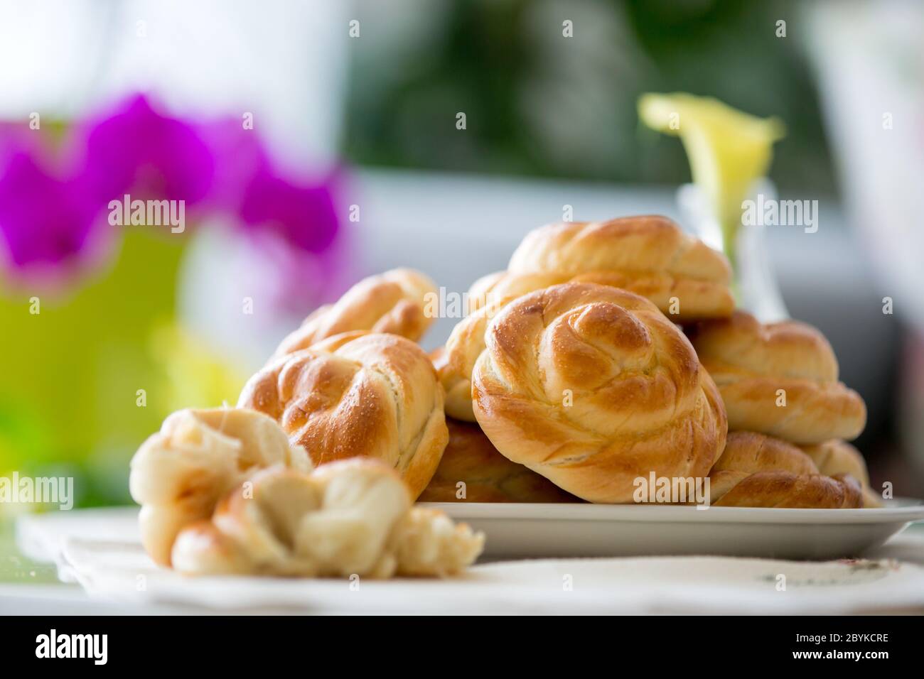 Bread buns in a plate on a table, vase with flower behind Stock Photo ...