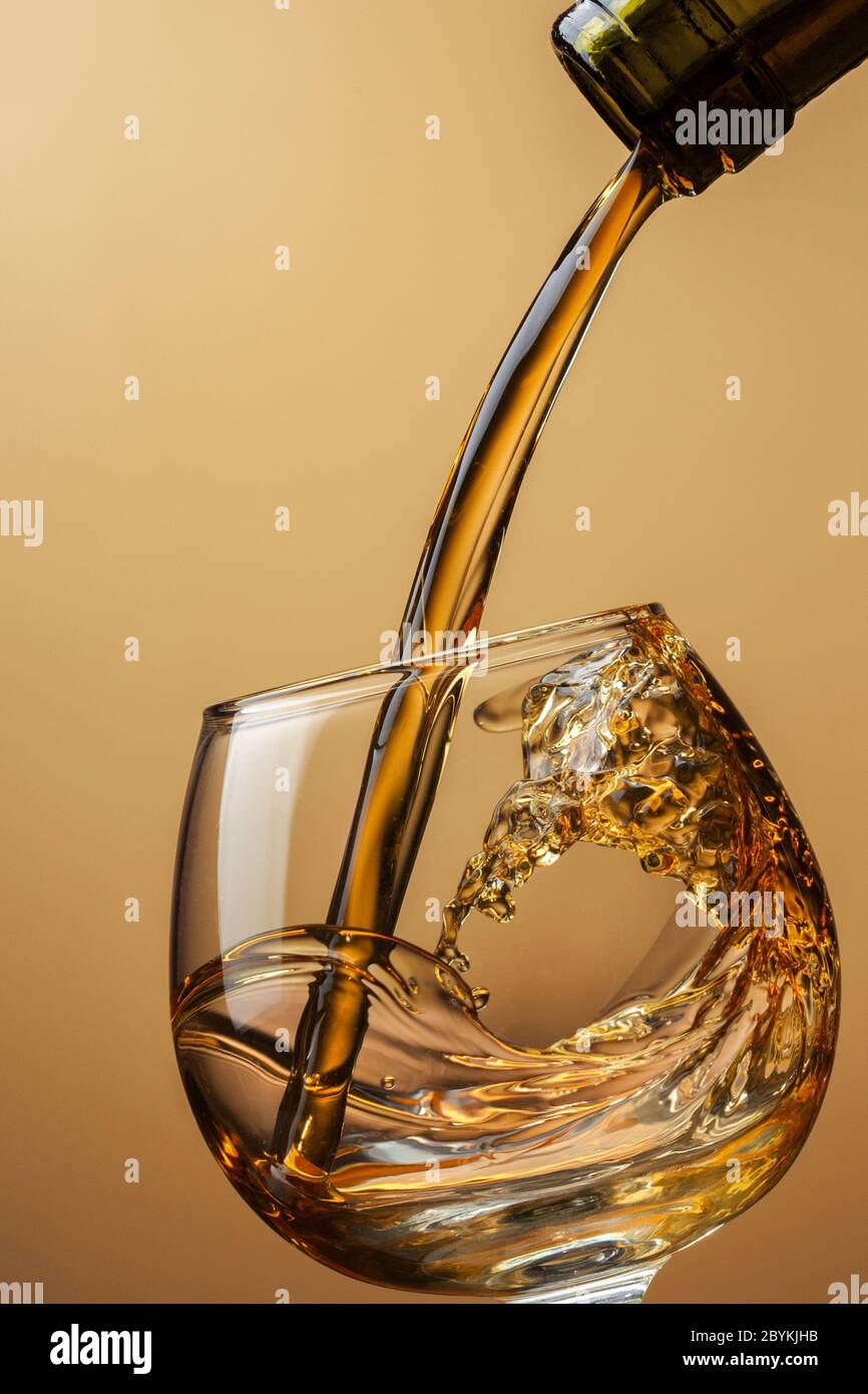 Cognac pouring from bottle into glass with splash on brown background ...