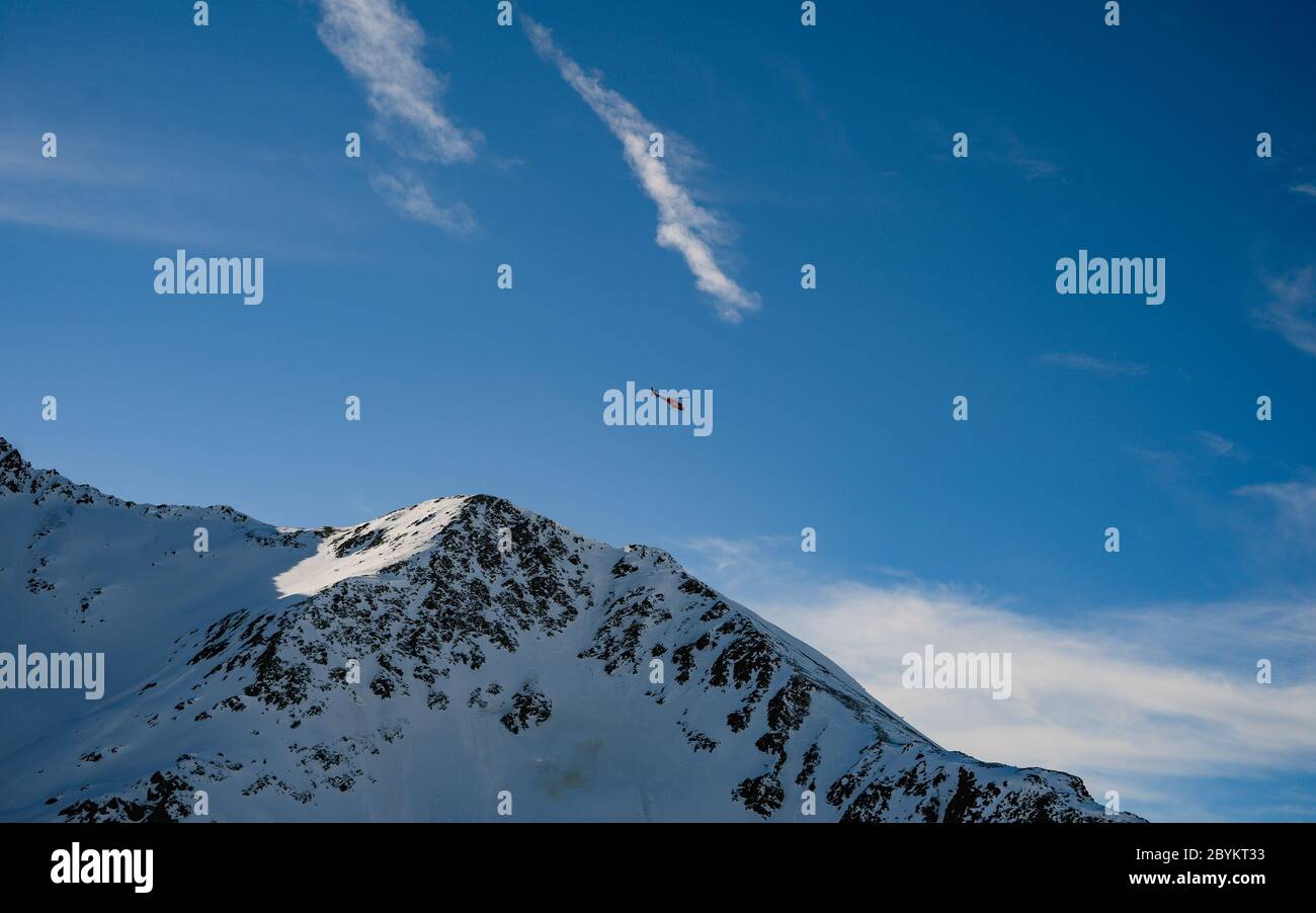 Red rescue helicopter flying over the view of the snowy rocks in Alpine ...