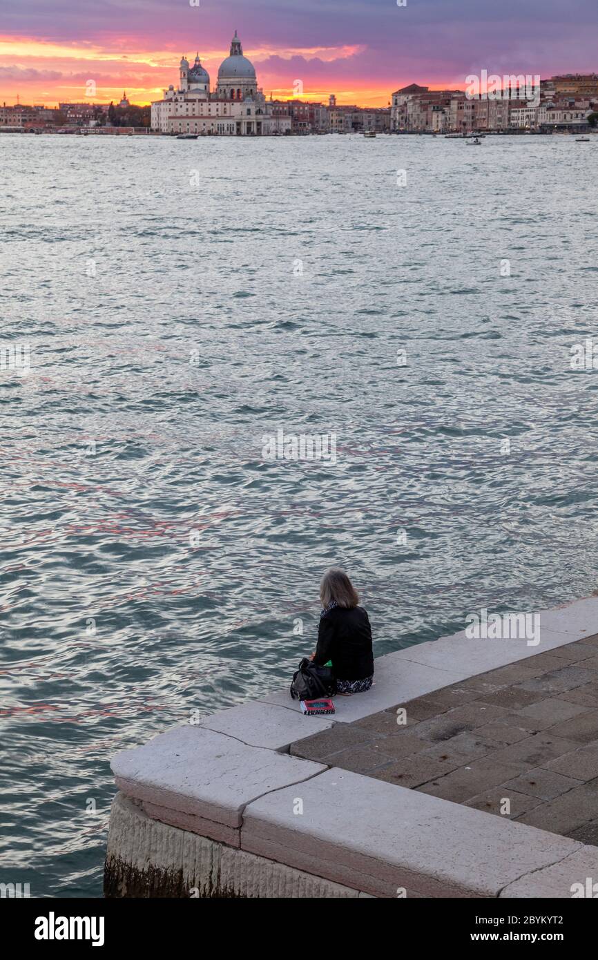 Lady sat on the quay along Riva degli Schiavoni, Venice, Italy gazing ...
