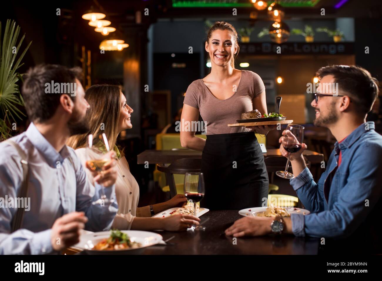 Pretty waiter woman serving group of friends with food in the restaura ...