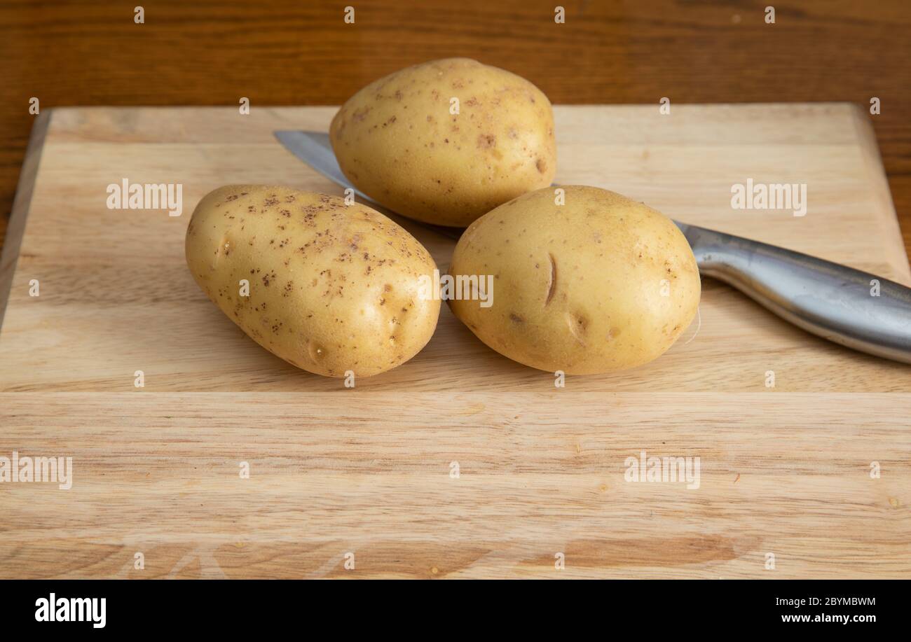 Potatoes waiting to be prepared on a wooden chopping board with a sharp ...