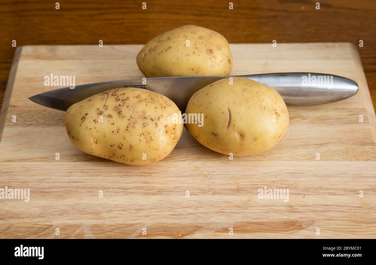 Potatoes waiting to be prepared on a wooden chopping board with a sharp ...