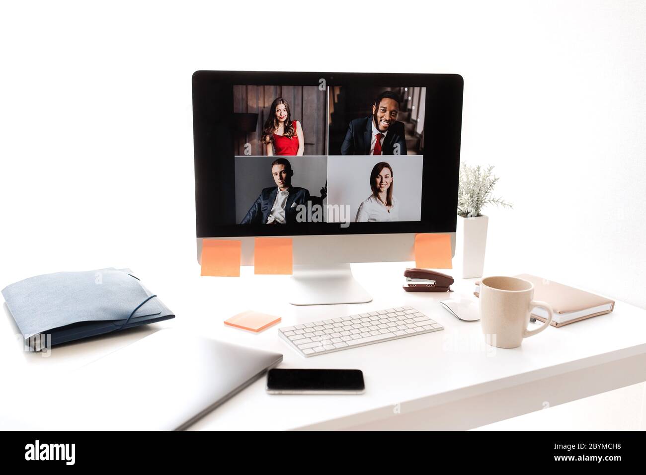 Monitor screen with video call and smartphone on a white office desktop ...