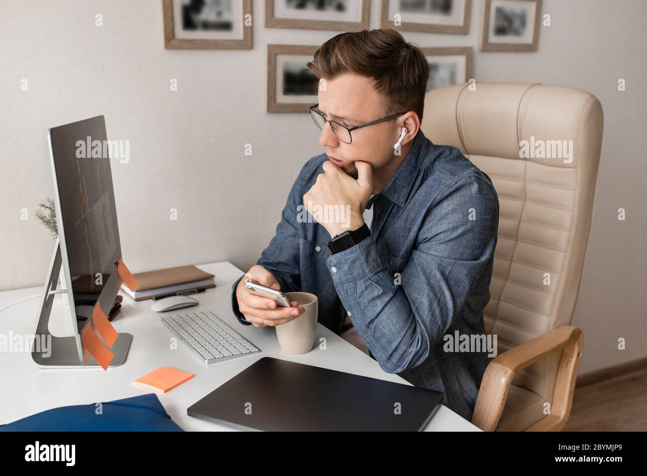 Young serious handsome white man working on a laptop from home using ...