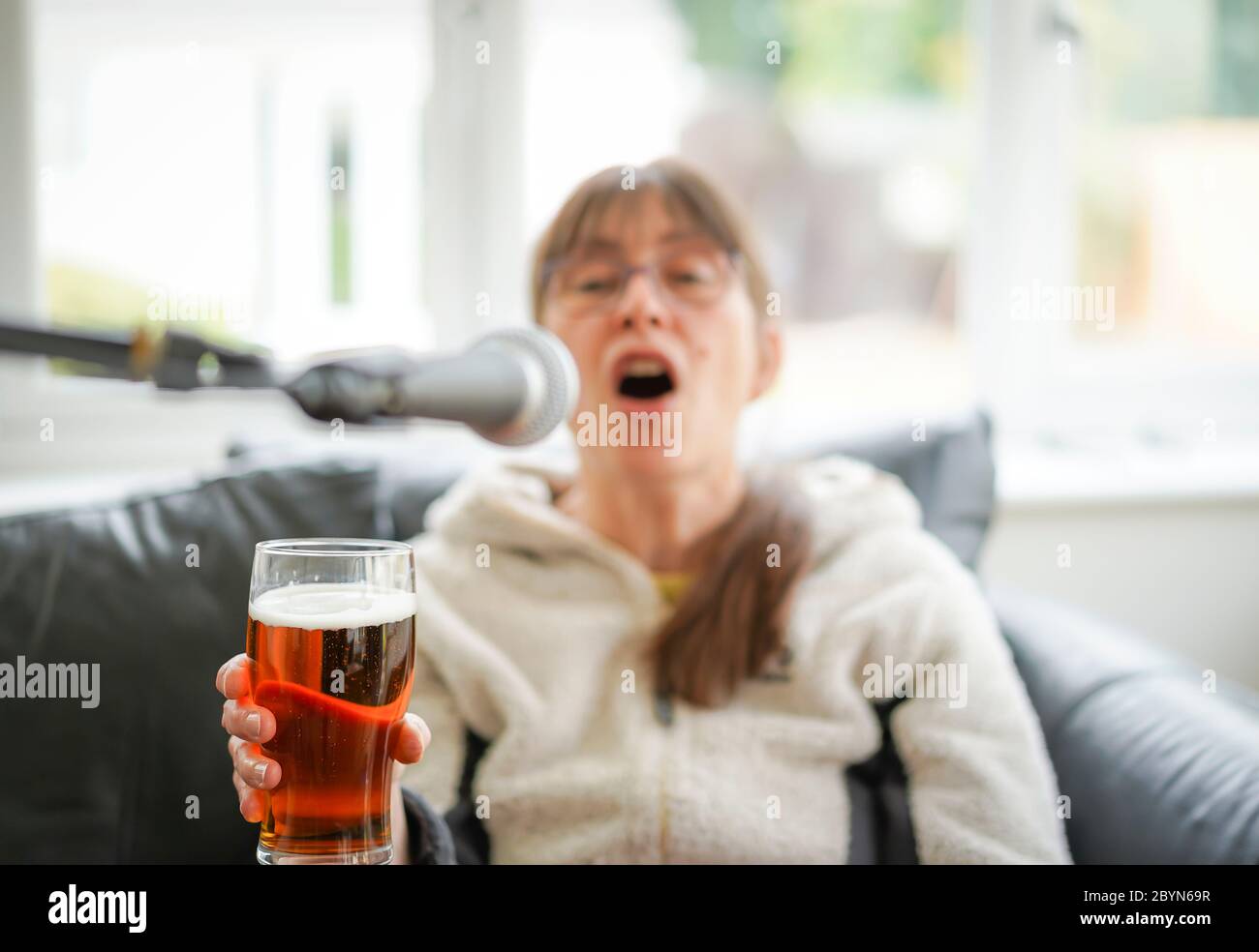 Isolated young woman drinking beer at home and singing into microphone ...