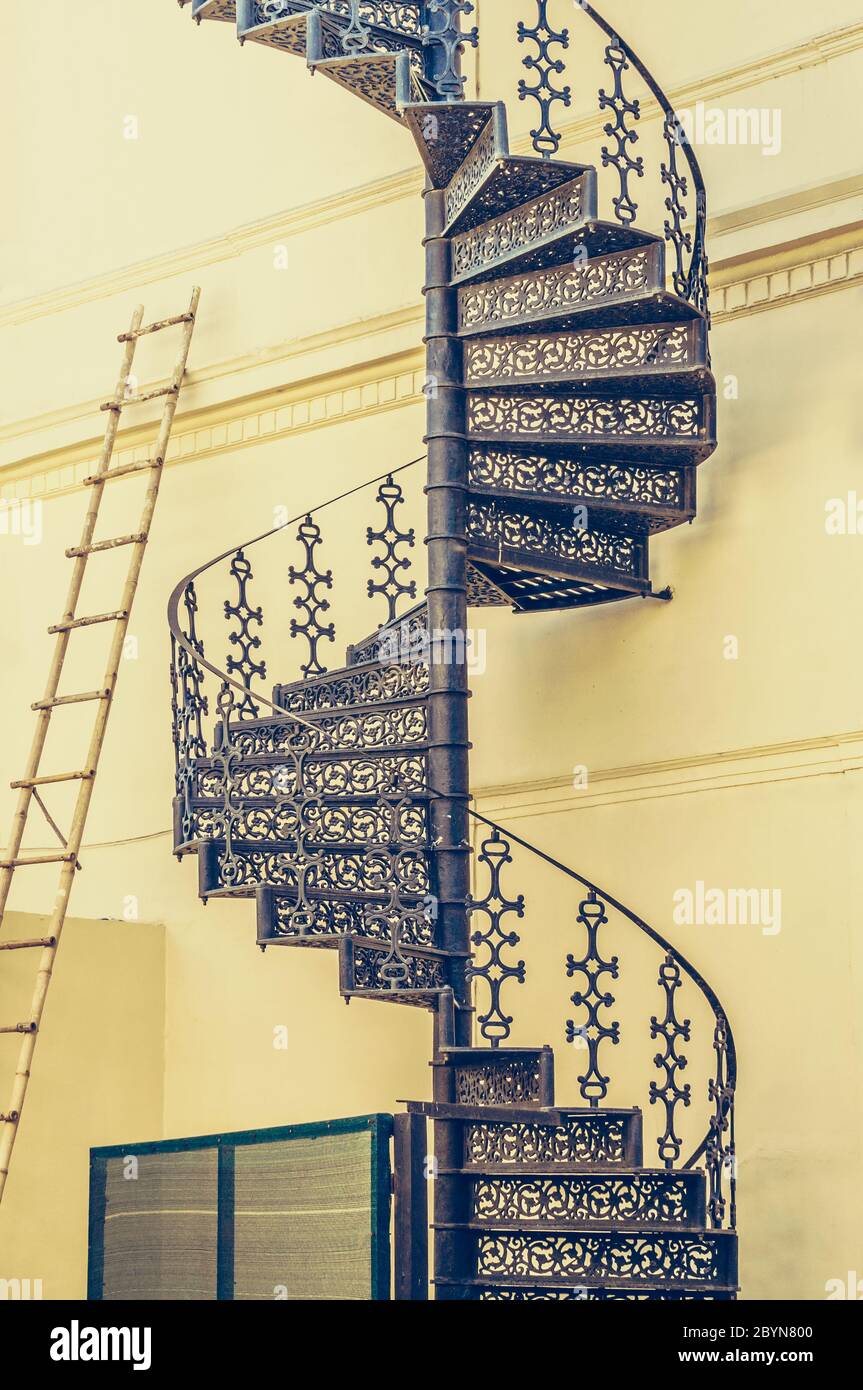 Vintage black wrought spiral stairs and bamboo ladder lean on yellow ...