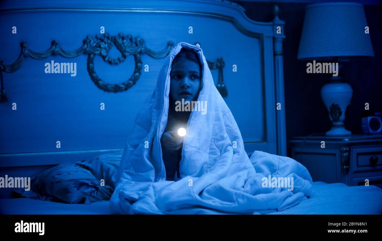 Portrait of afraid of nightmares little girl hiding under blanket in ...