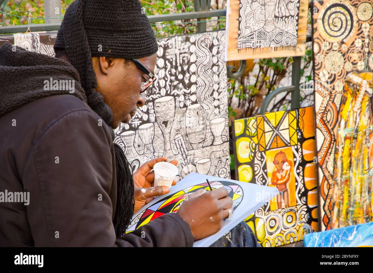 An African street painter paints his colorful paintings in a square in ...