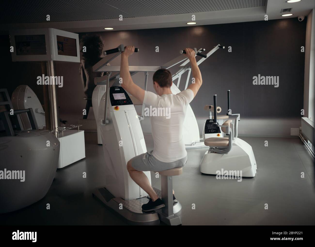 Modern gym - a young man in white t-shirt sitting on the strength ...