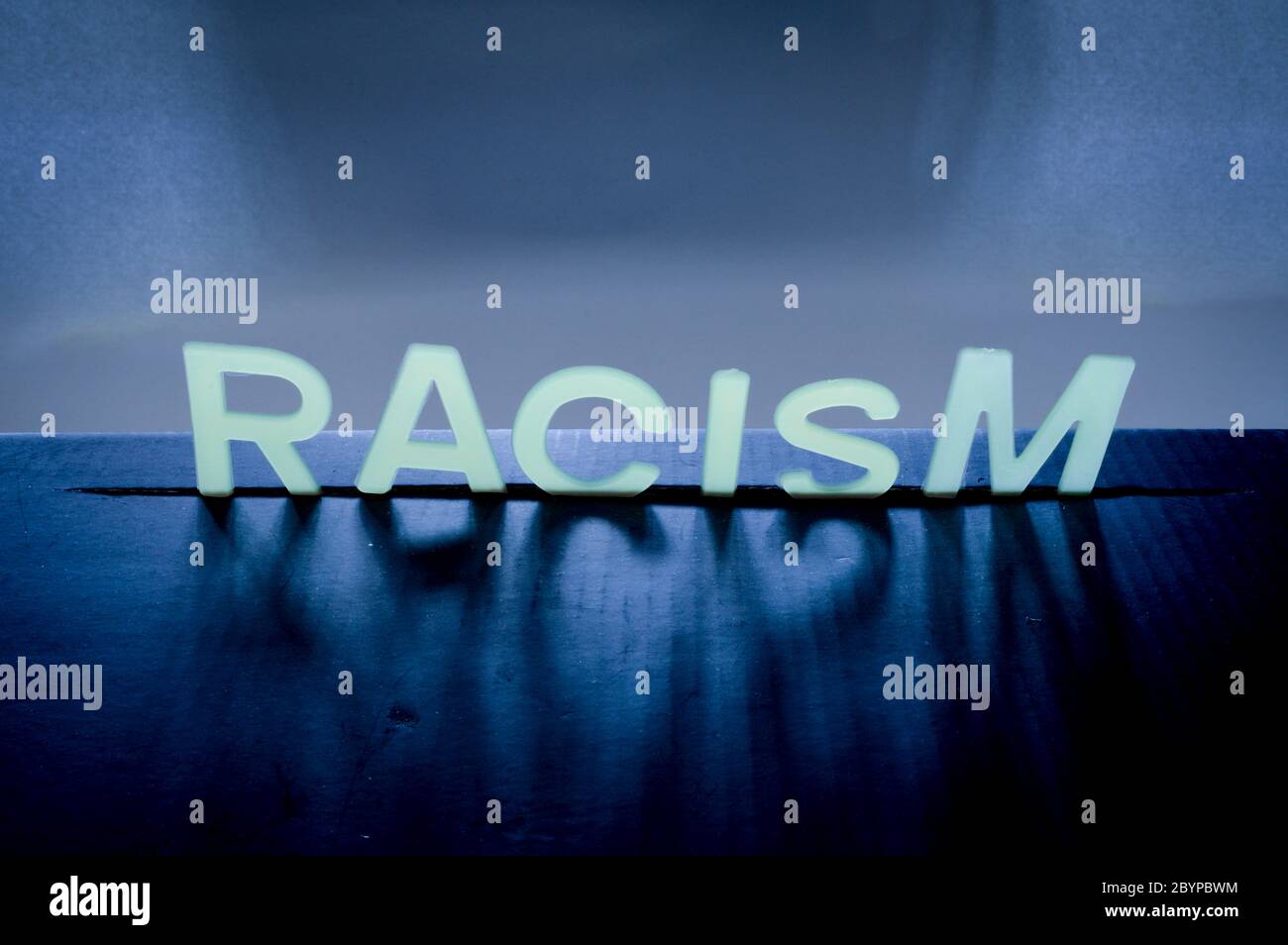 The shadow of racism. Back lit word with shadows. Concept against ...