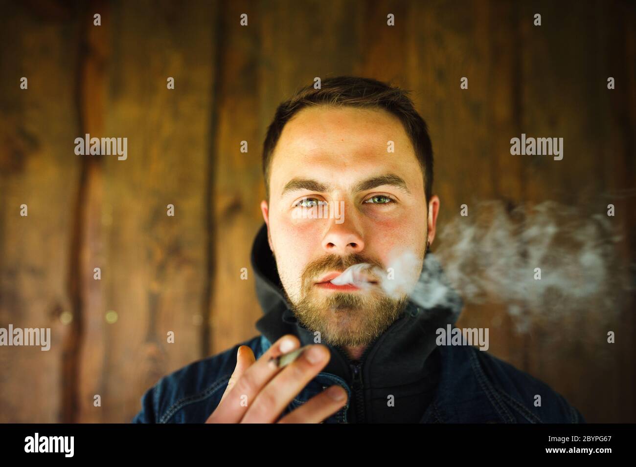 Portrait of a real young man smoking in front of wooden wall, natural ...