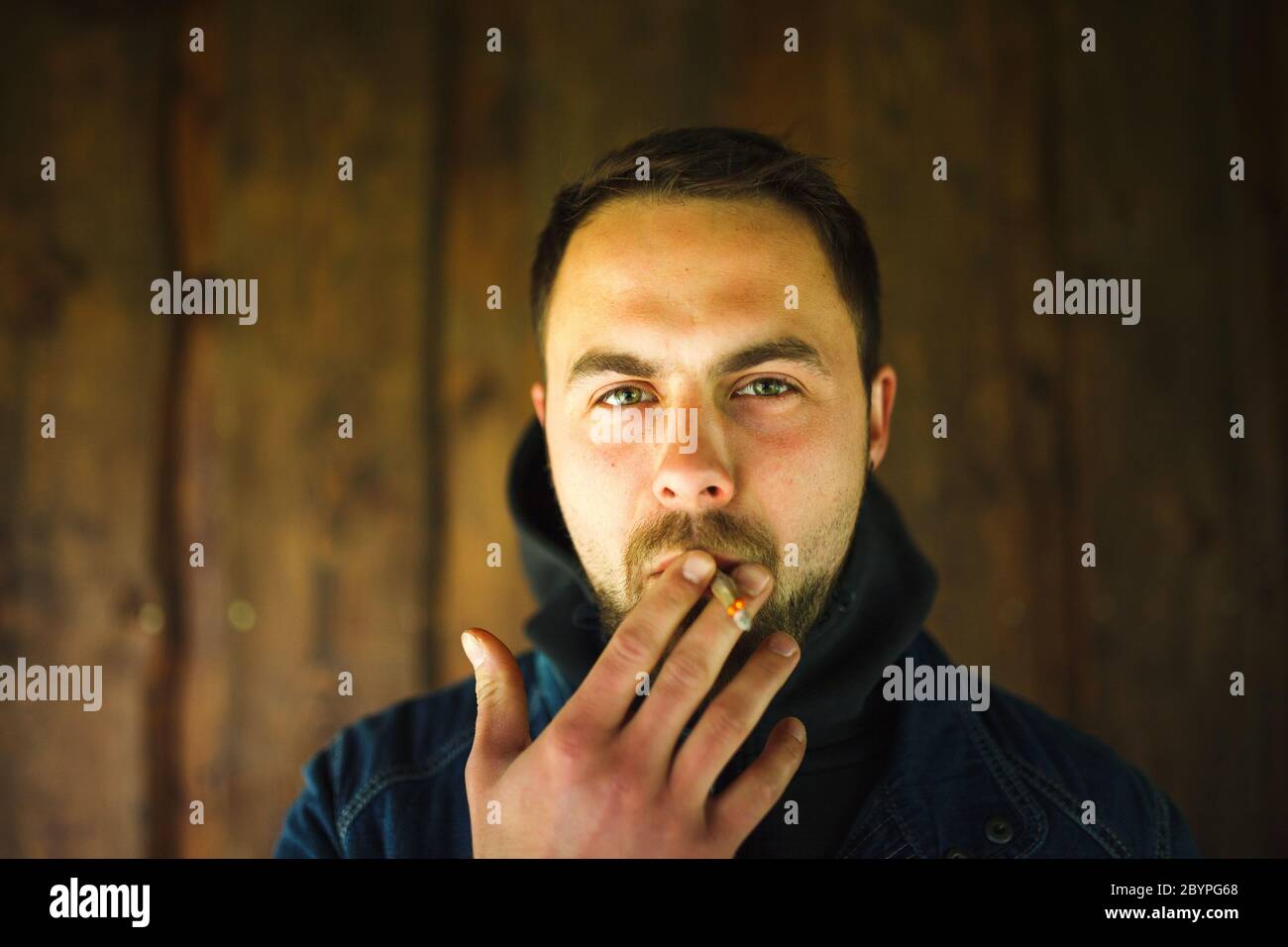 Portrait of a real young man smoking in front of wooden wall, natural ...