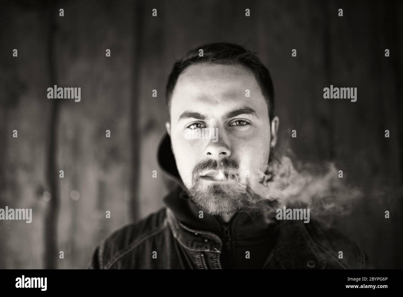 Portrait of a real young man smoking in front of wooden wall, natural ...