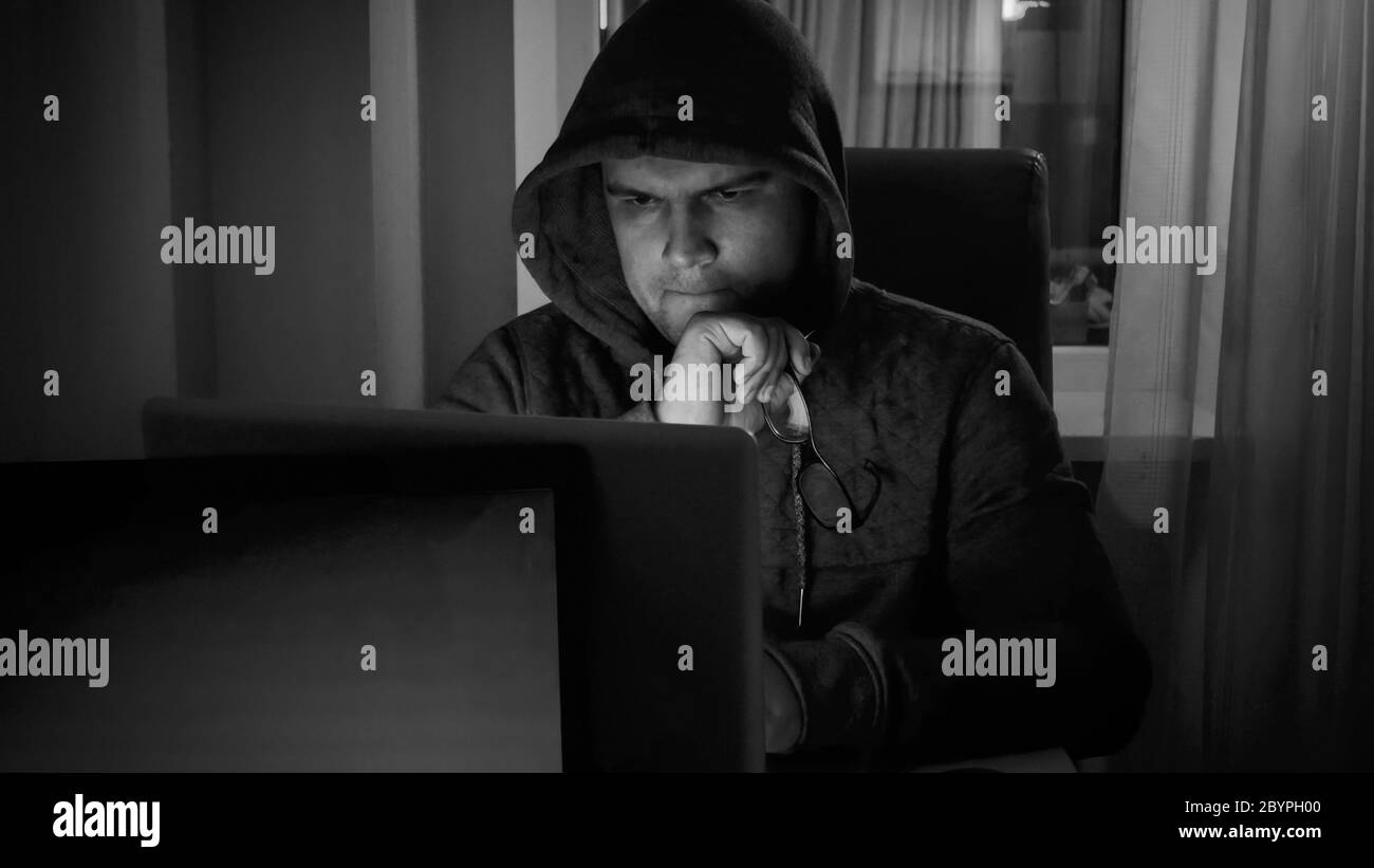 Black and white portrait of male hacker in hood working on computer at ...