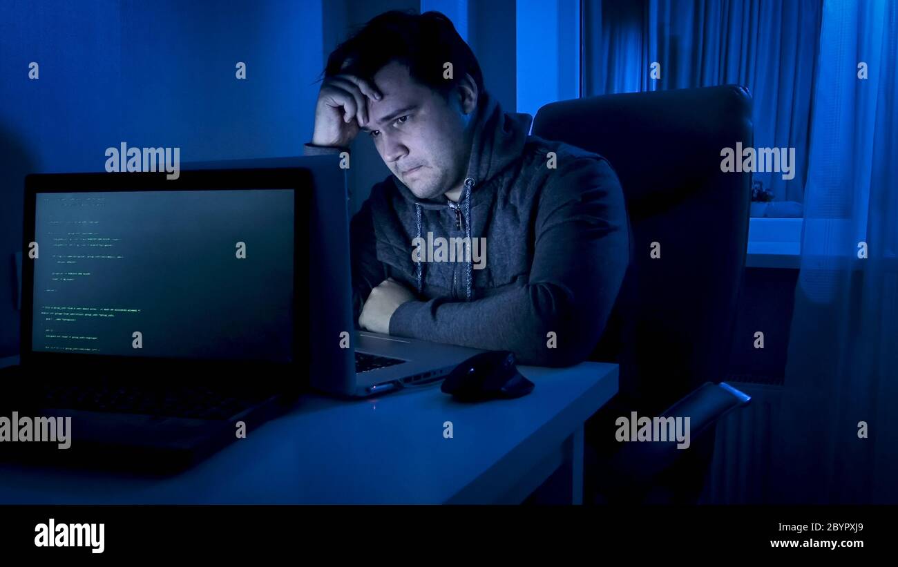 Uoset stressed male programmer working on computer in office at night ...