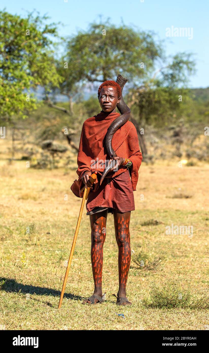 Young Masai warrior is standing in the savannah in traditional clothes ...