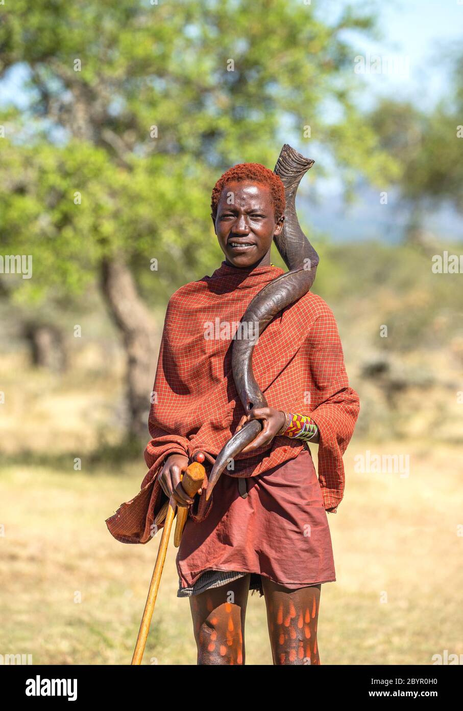 Young Masai warrior is standing in the savannah in traditional clothes ...