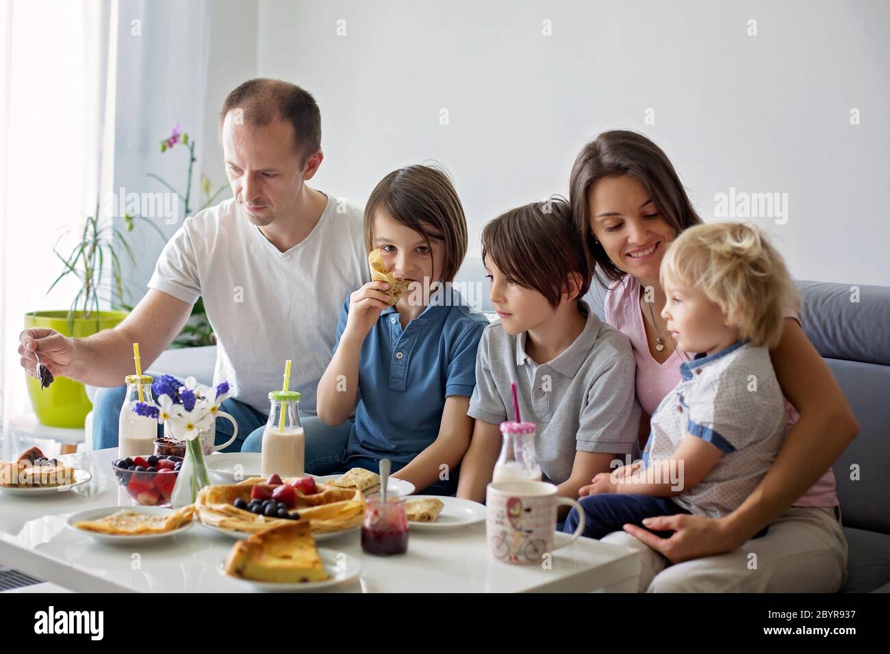 Happy family, having pancakes for breakfast, eating in living room ...