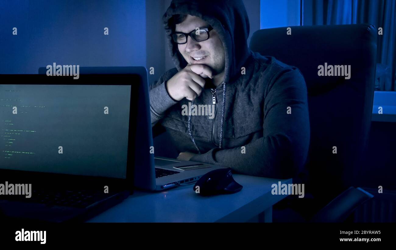 Portrait of smiling male hacker looking on laptop after stealing money ...