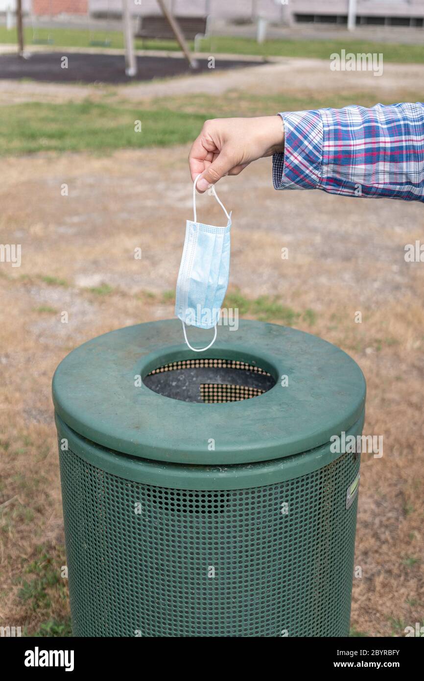 Female hand throwing Medical face mask in the trash can of a park ...