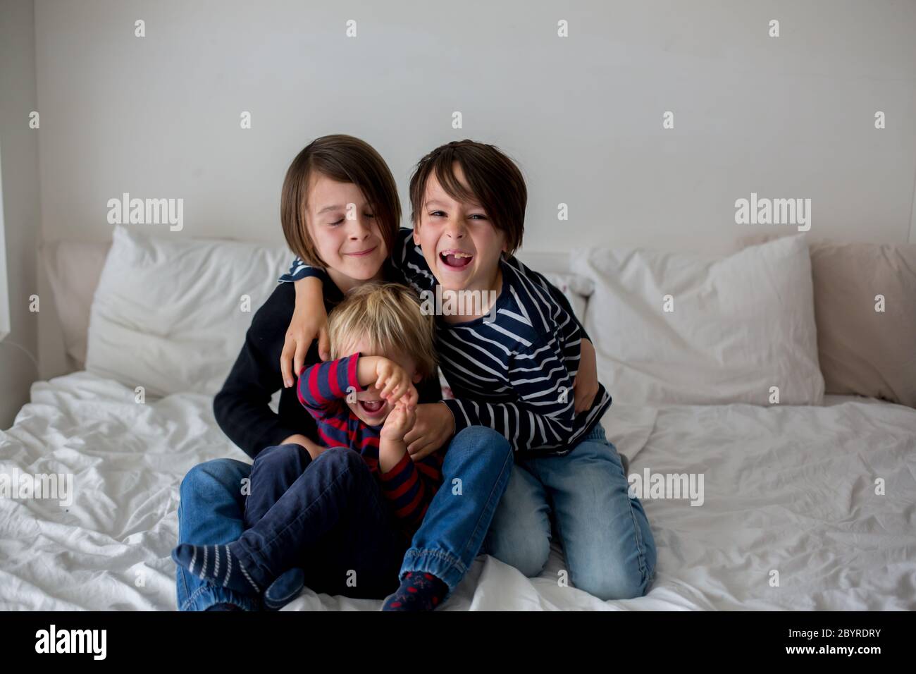 Three children, boy brothers, laughing in bed, gigling and tickling ...