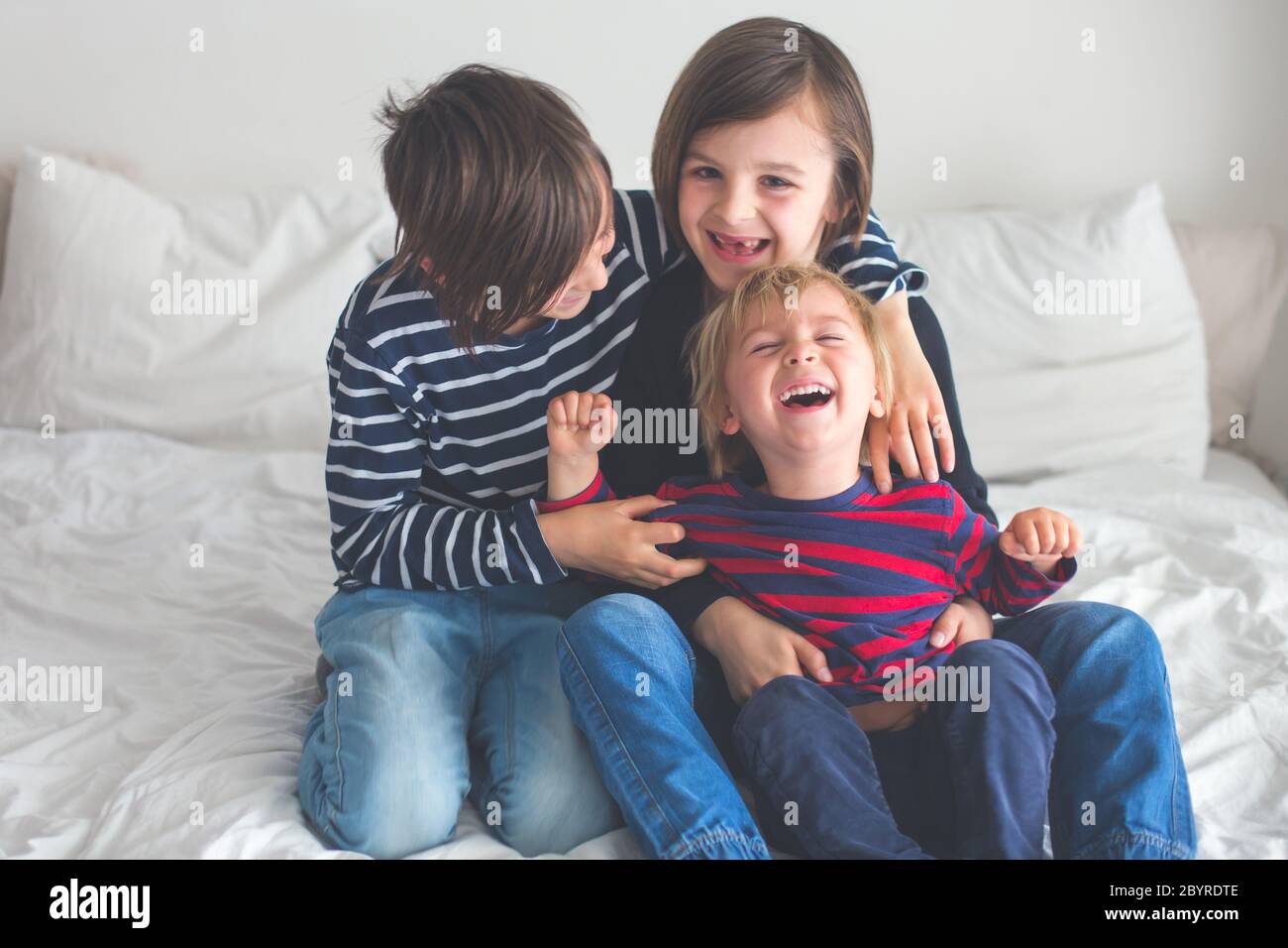 Three children, boy brothers, laughing in bed, gigling and tickling ...