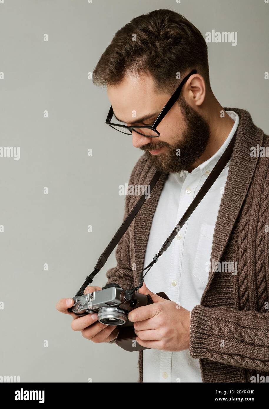Confident hipster photographer with camera on a strap posing isolated ...