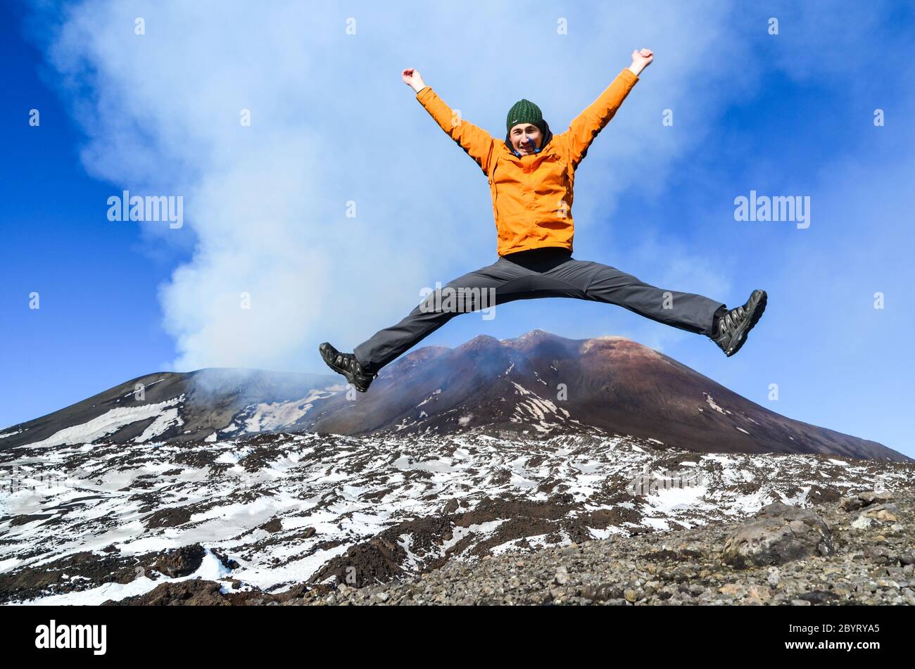 Man in orange jacket jumping on top of Mount Etna, Sicily, Italy, with ...