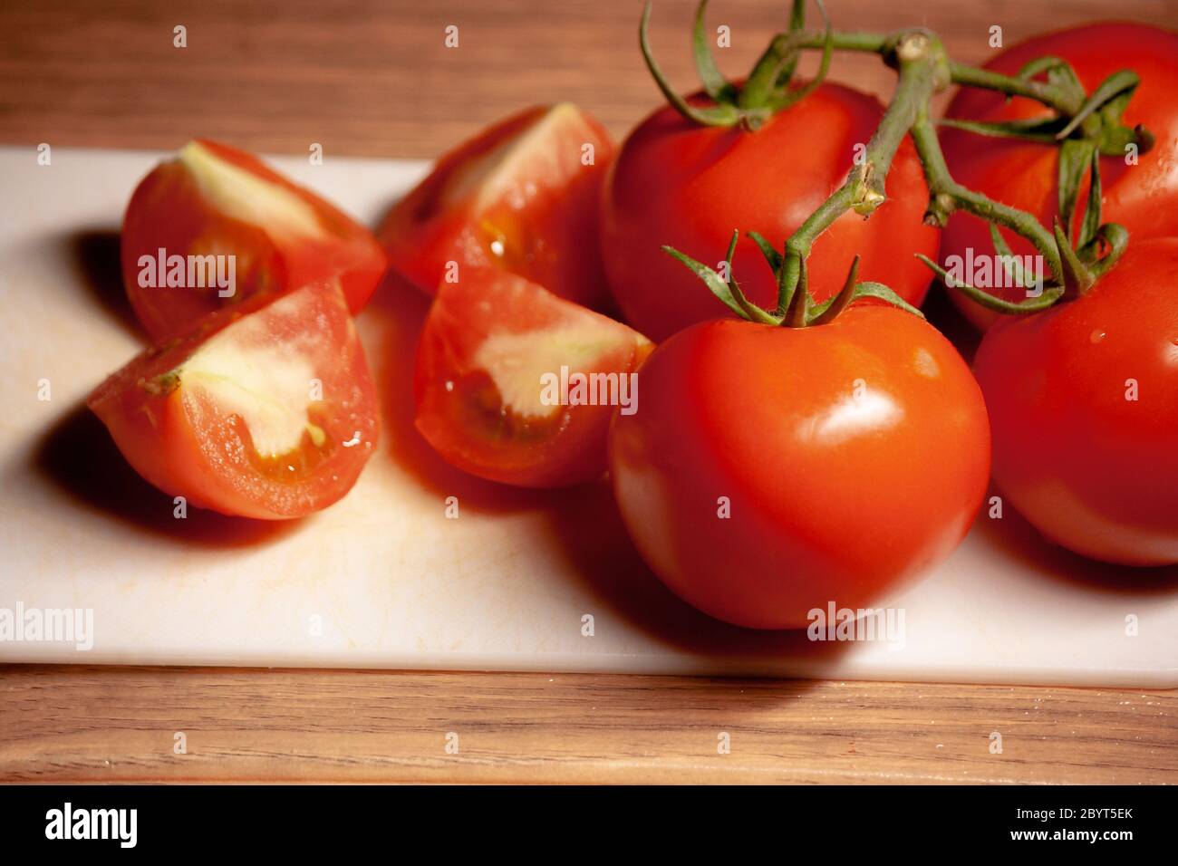 Tomato in four pieces with bunch of whole tomatoes on white chopping ...