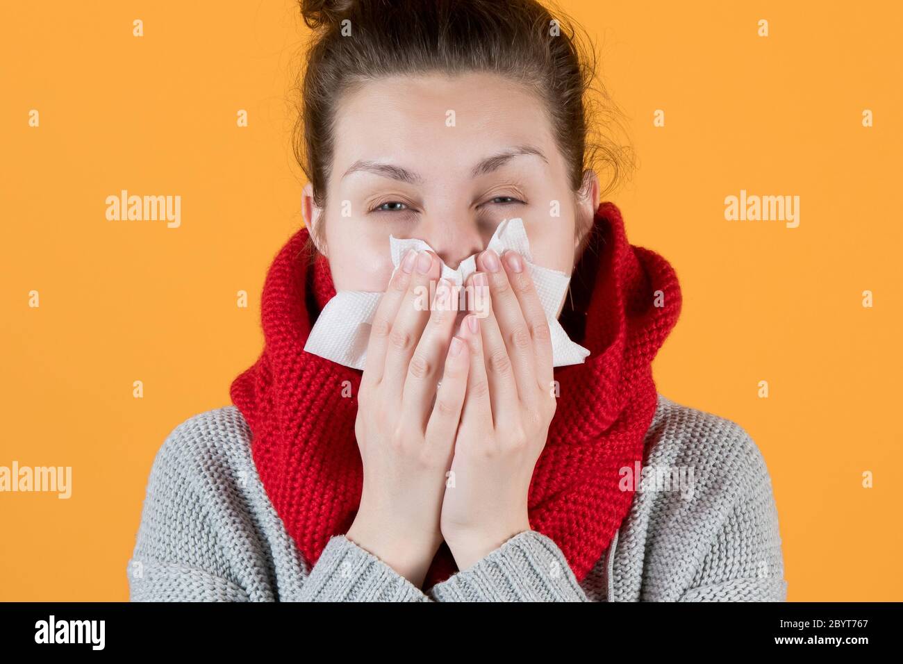 a sickly-looking girl in a scarf squints, sneezing into a scarf Stock ...