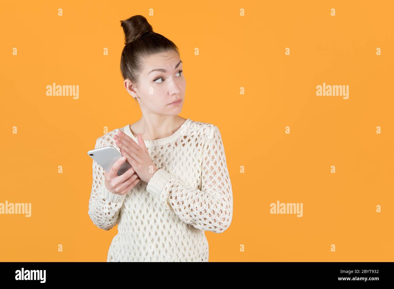 girl looks inquiringly at an empty place, covering her phone screen ...