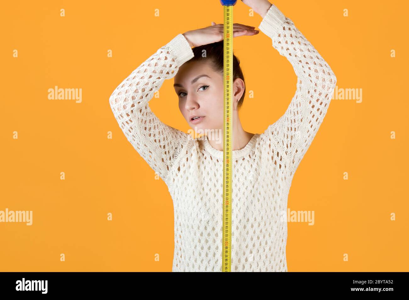 girl measures her height, holding a measuring tape nearby and looks at ...