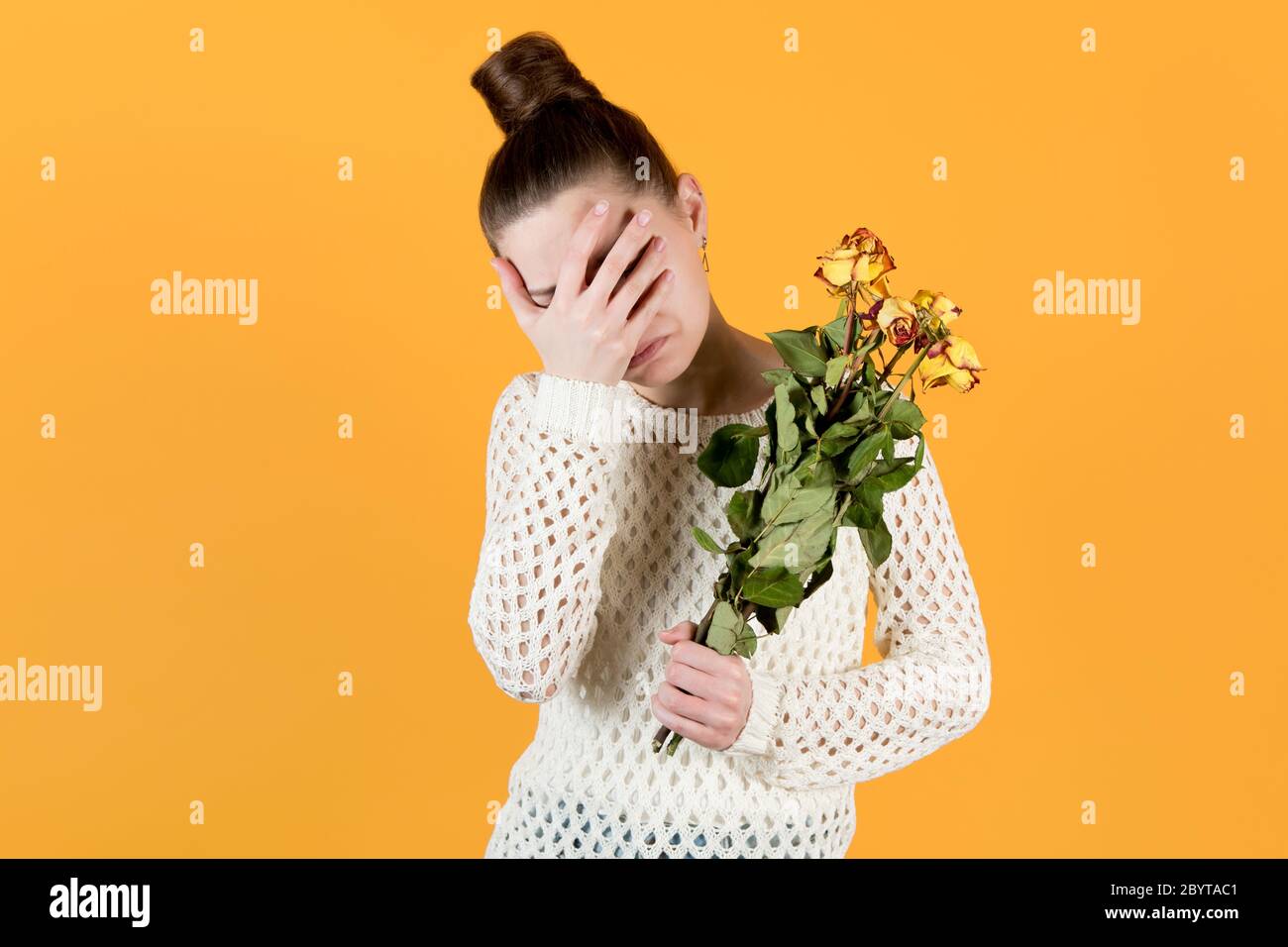 girl covers her face in crying, she holds withered flowers in her hands ...