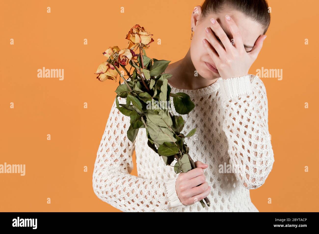 girl covers her face in crying, she holds withered flowers in her hands ...