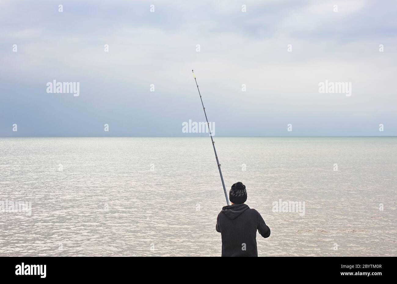 Man in black fishing into a big sea Stock Photo - Alamy