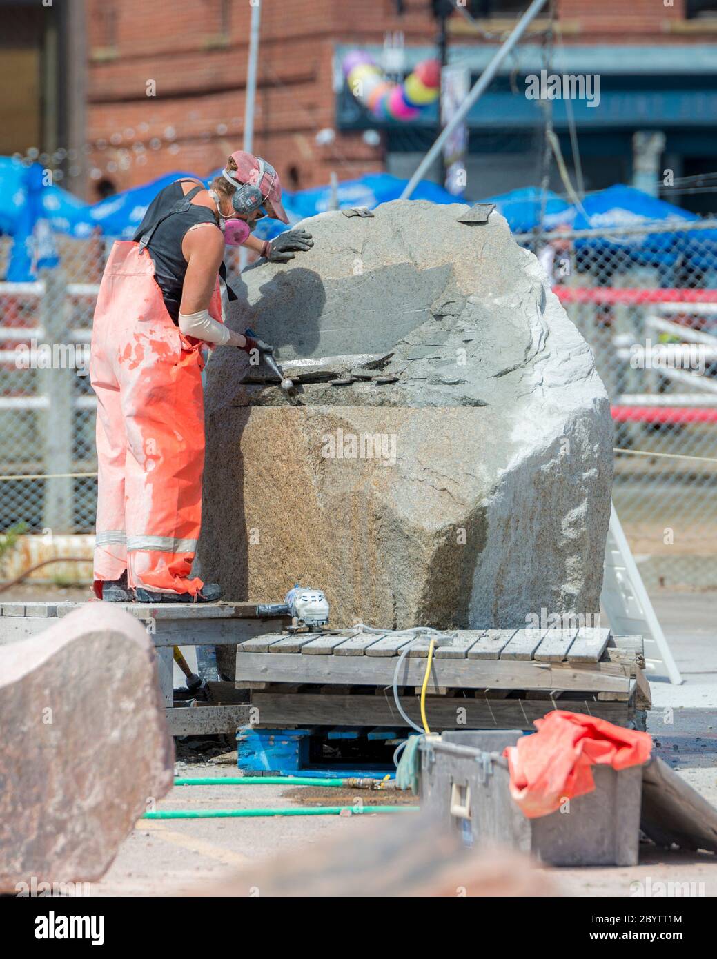 An artist works on a large block of stone at Sculpture Saint John, a ...