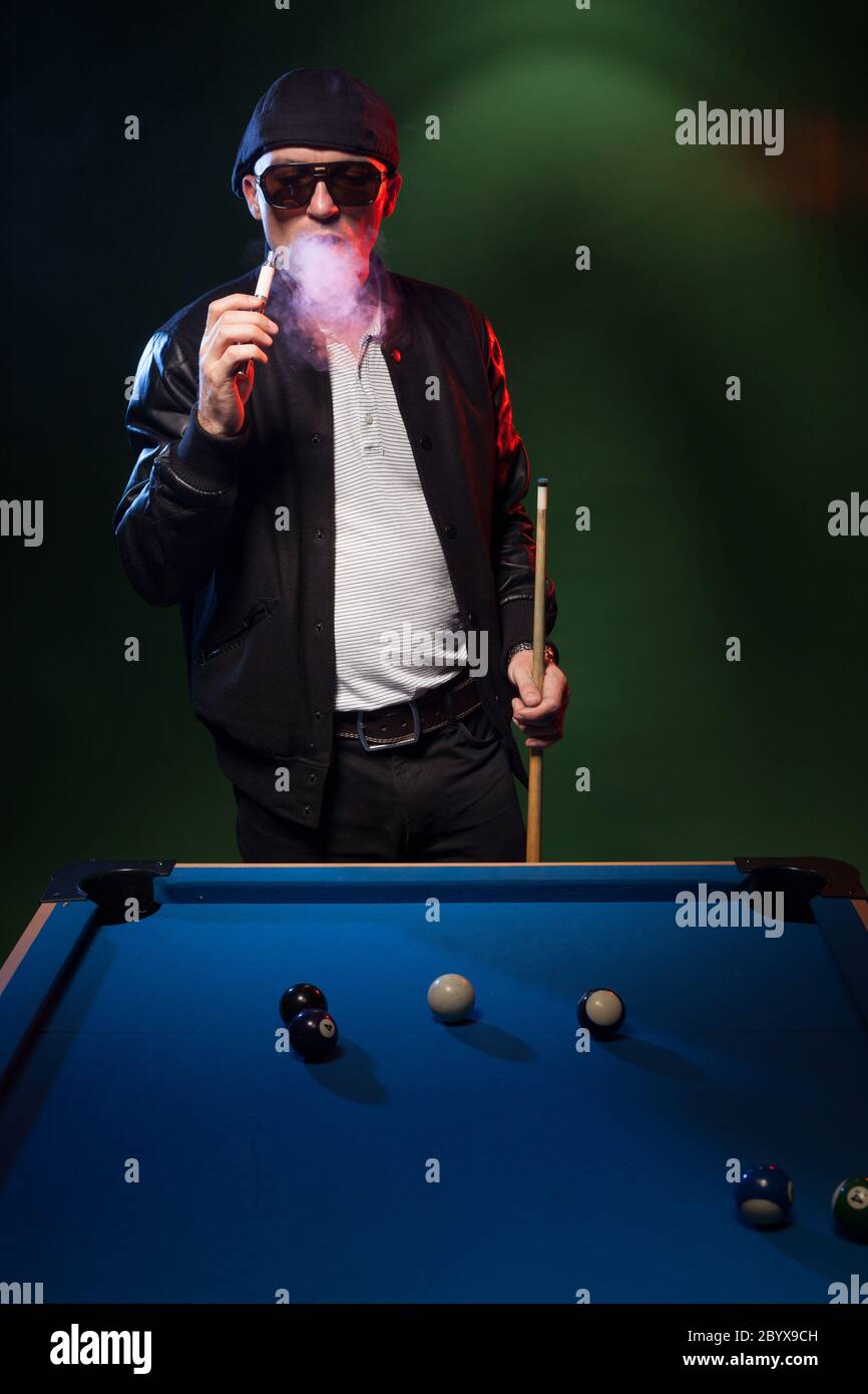 Man playing pool in a club smoking a cigarette Stock Photo - Alamy