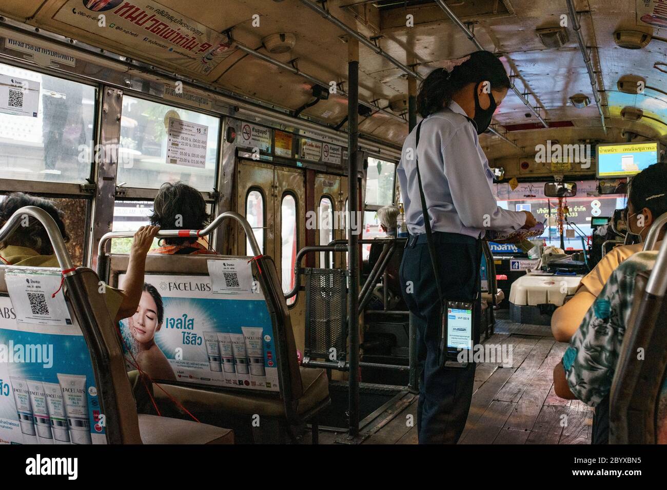 A Thai bus conductor wearing a face mask as a precaution, collecting a ...
