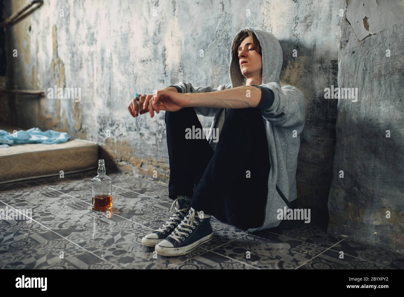 Junkie with syringe in hand sitting on the floor after dose, bottle of ...