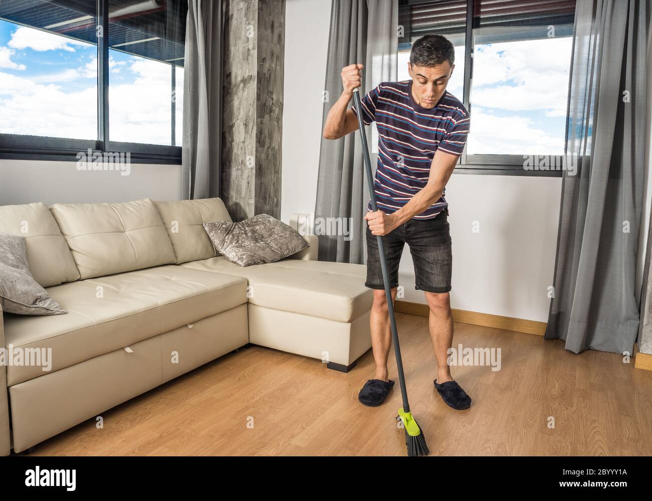 Man in casual clothes and slippers sweeping his living room. Full body ...