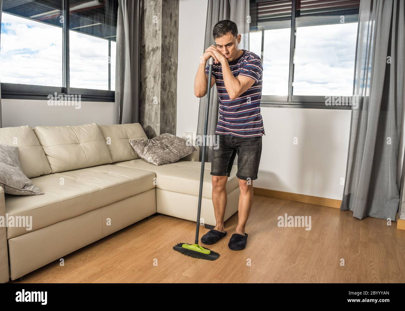 Sad and pensive man sweeping up his living room with casual clothes and ...