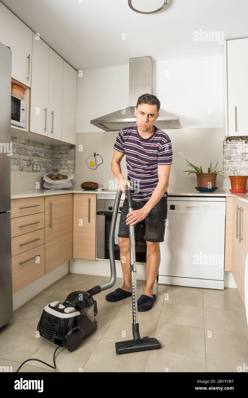 Man vacuuming the kitchen with a bored gesture. Full body Stock Photo ...