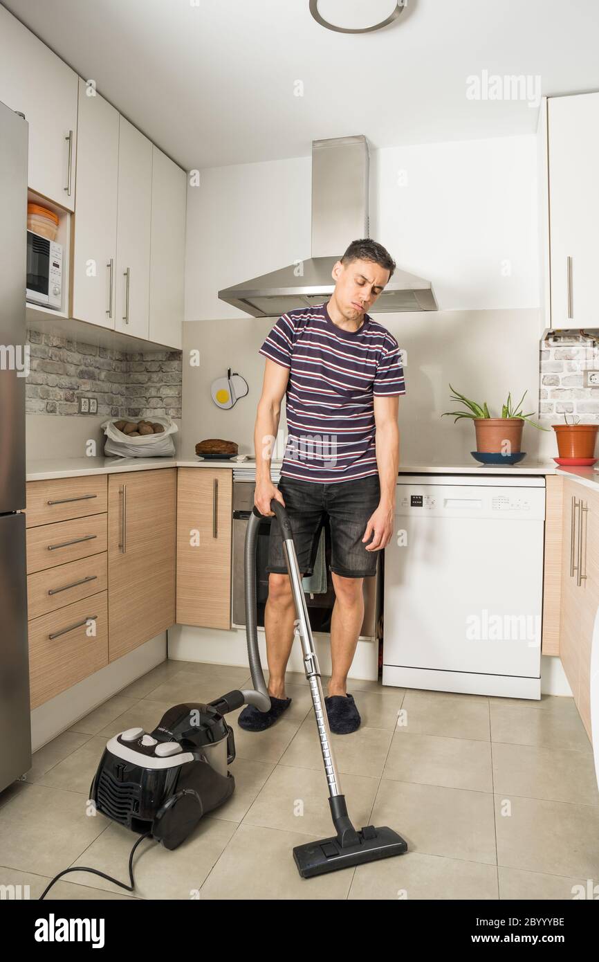 Man vacuuming the kitchen with a bored gesture. Full body Stock Photo ...