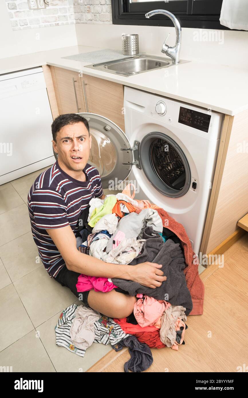 Man in casual clothes worried next to the washing machine, with a lot ...