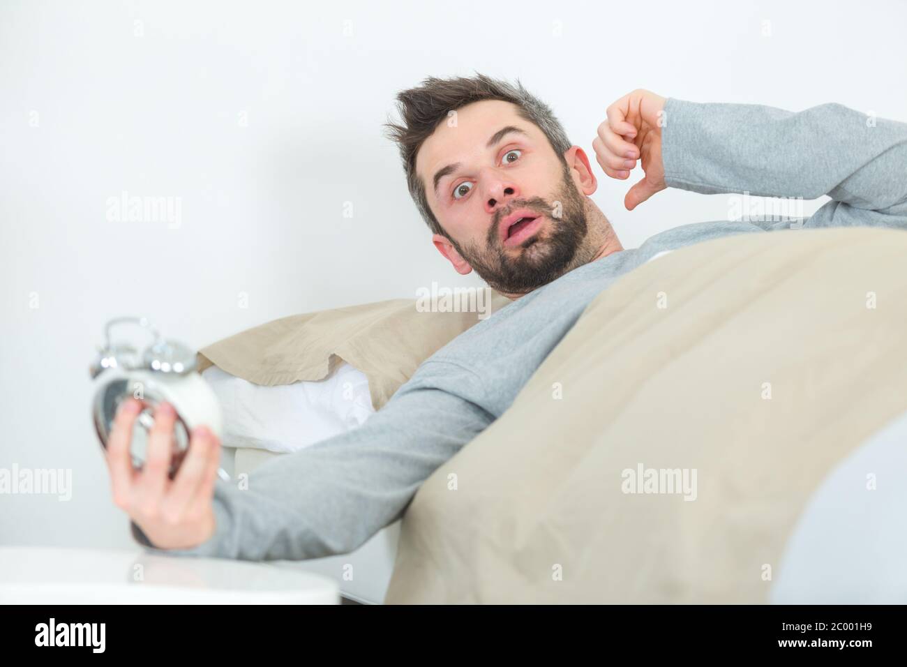 man in bed looking in shock at time on clock Stock Photo - Alamy