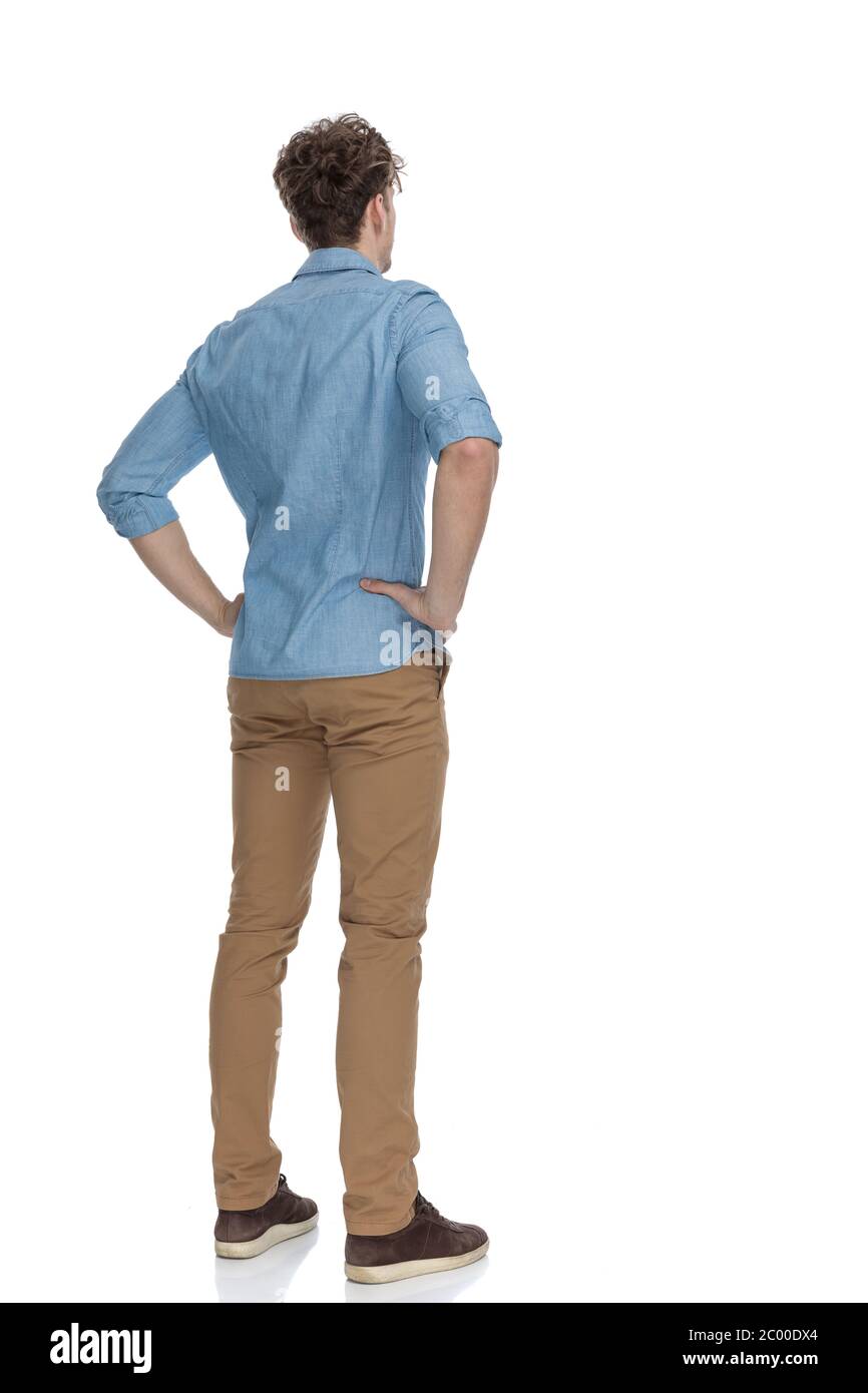 back view of concerned casual guy holding hands on hips and thinking ...